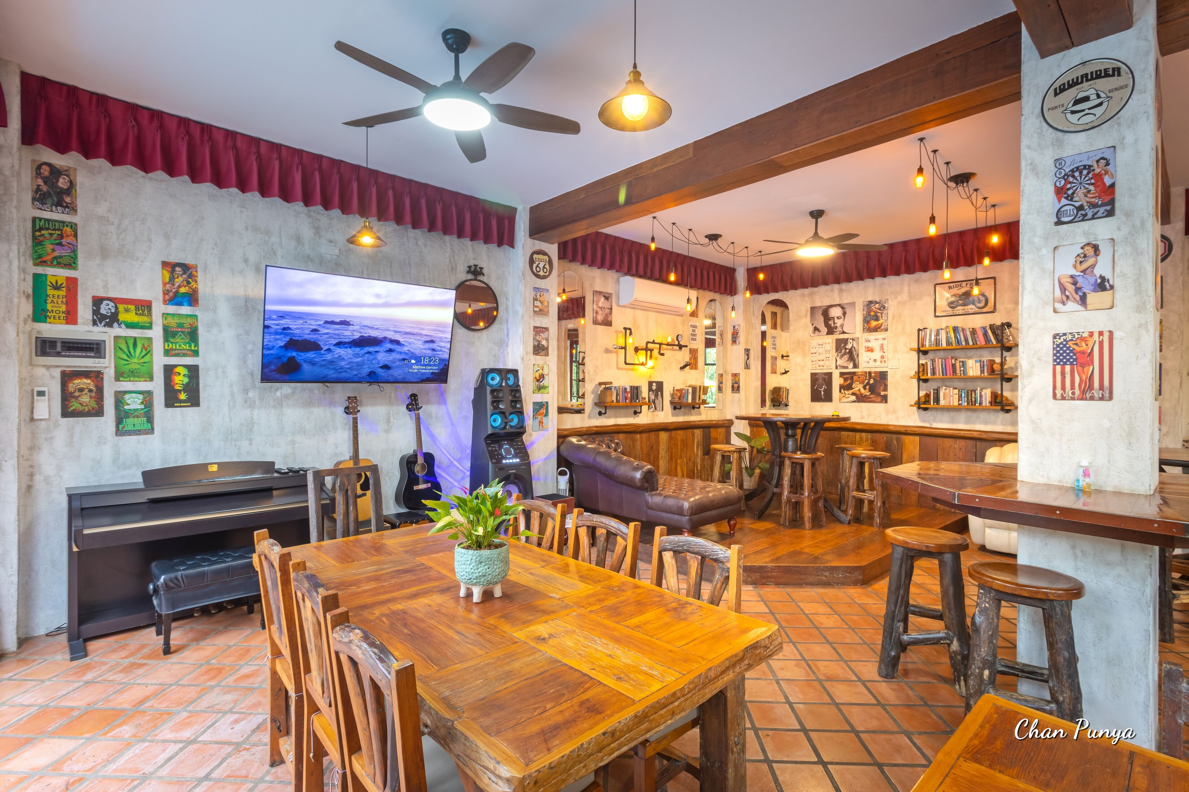 Um espaço de bar acolhedor com uma mesa de madeira, banquetas e uma televisão na parede.