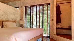 Quarto com cama de madeira, mesa de cabeceira, janela com persianas, banheiro com chuveiro e piso ladrilhado.