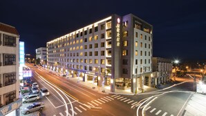 Hotel de vários andares com fachada moderna, janelas iluminadas e área de entrada bem iluminada.