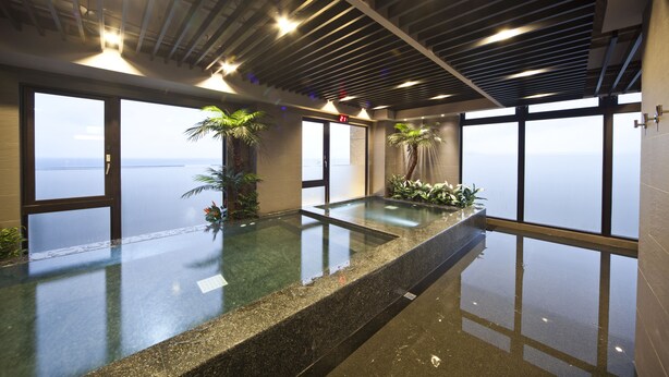 Piscina interior moderna com fundo de vidro, janelas amplas e plantas em vasos.