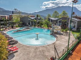 Uma piscina com escorrega aquático, rodeada por espreguiçadeiras e guarda-sóis, com montanhas ao fundo.