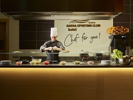 Um chef preparando comida numa cozinha com um letreiro que diz "Garda Sporting Club hotel Chef for you!".