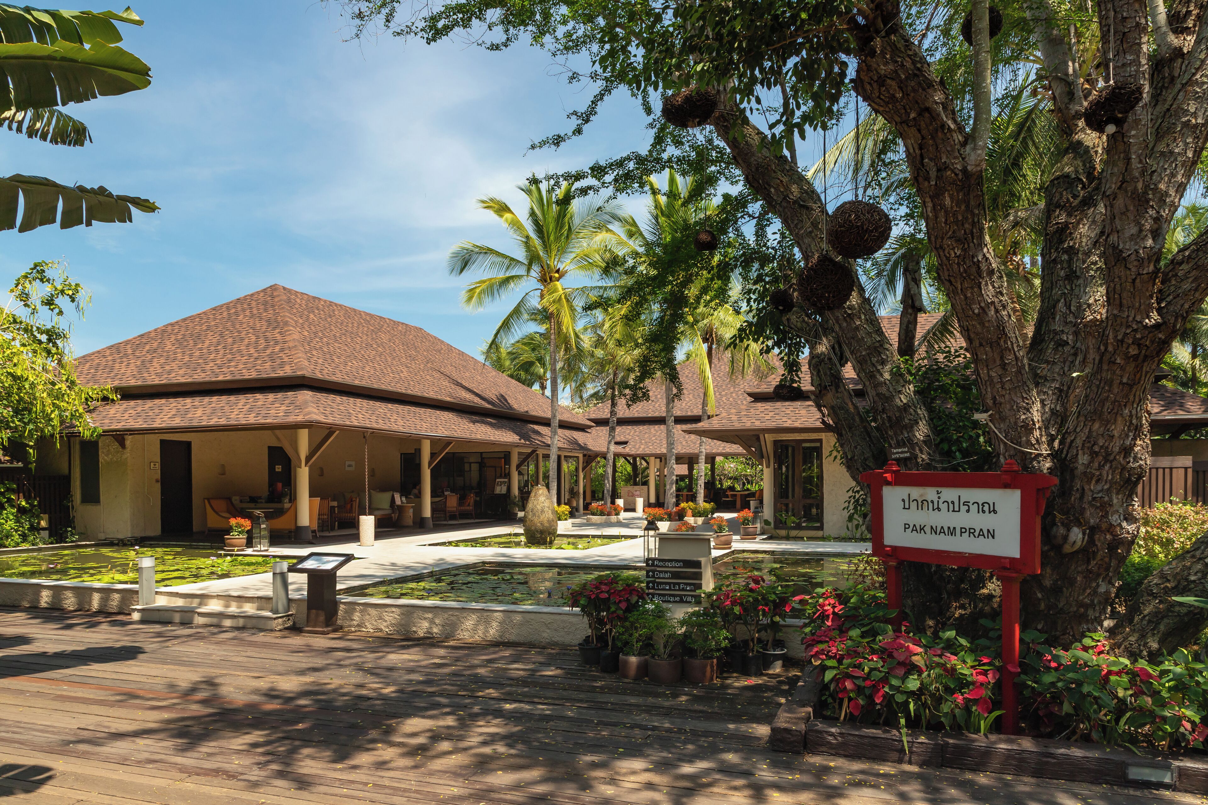 Um resort com um alpendre coberto, palmeiras e uma placa com a inscrição 'Pak Nam Pran'.