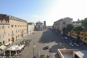 Uma praça ampla com edifícios históricos, mesas ao ar livre e carros estacionados.