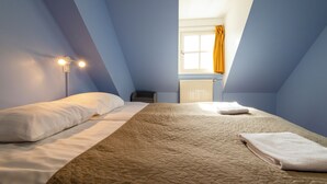Quarto com cama, almofadas, mesa de cabeceira e janela com cortinas.
