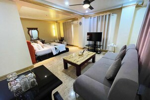 Quarto de hotel com sala de estar, sofá, mesa de centro, televisão e cama com mesa de cabeceira.