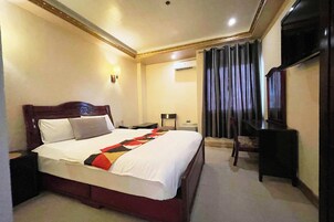 Quarto de hotel com cama grande, mesas de cabeceira, escrivaninha, cadeira, televisão e cortina.