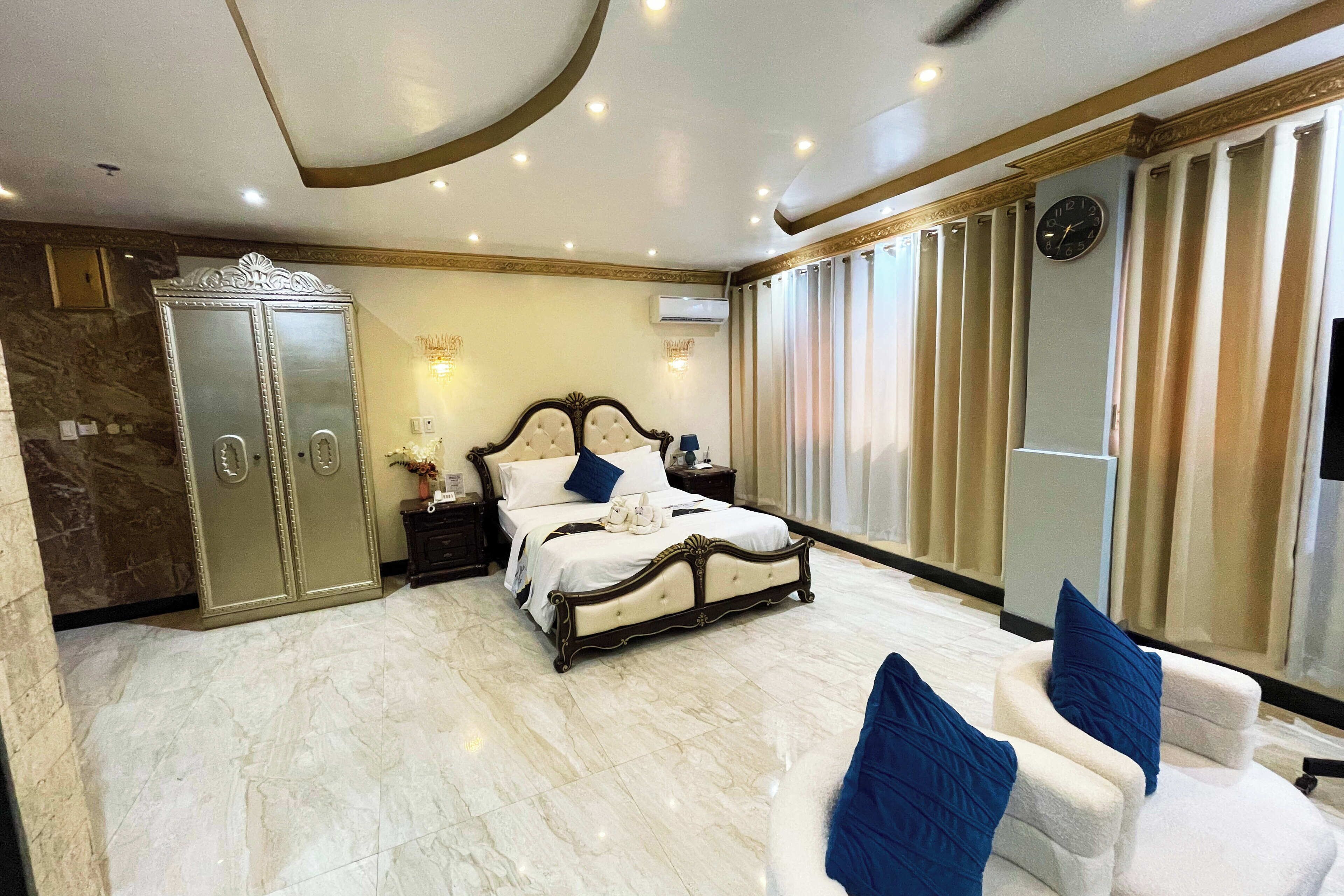Quarto espaçoso com cama grande, guarda-roupa e um espaço de estar com almofadas azuis.