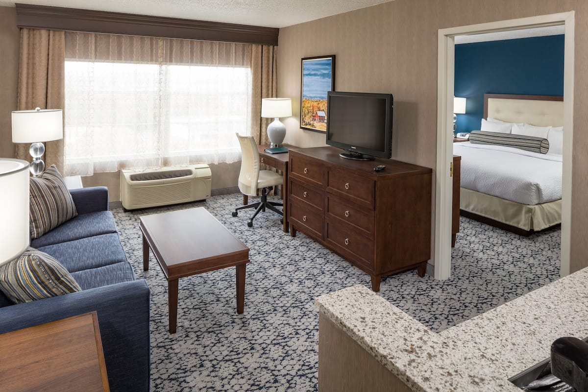Quarto de hotel com sofá, escrivaninha, televisão, cama e janela com cortinas.