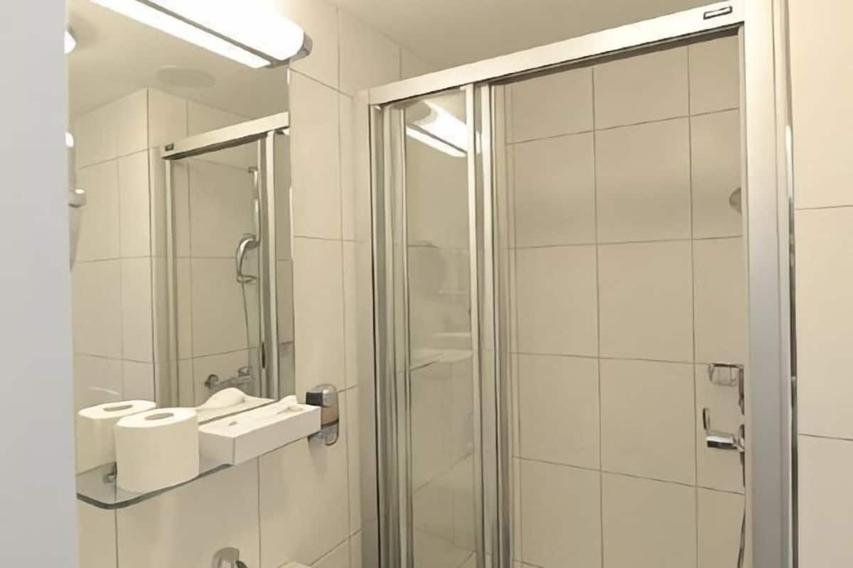 Um banheiro moderno com box de vidro, espelho e porta-papel higiênico.