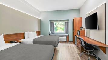 Quarto de hotel com duas camas, uma escrivaninha, uma televisão e janela com vista para o verde.