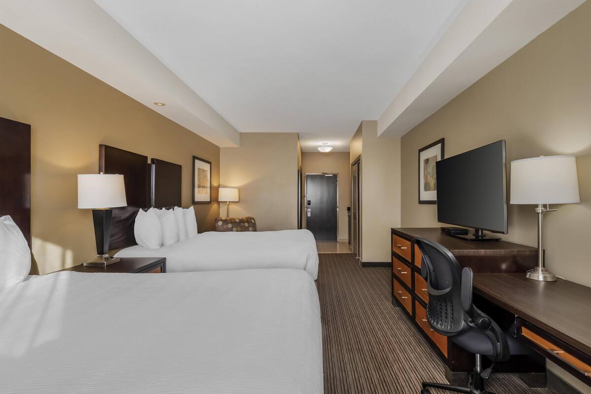 Quarto de hotel com duas camas, uma mesa, uma televisão e uma cadeira.