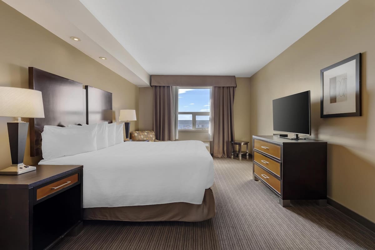 Quarto de hotel com uma cama grande, televisão, escrivaninha com luminária e janela com cortinas.