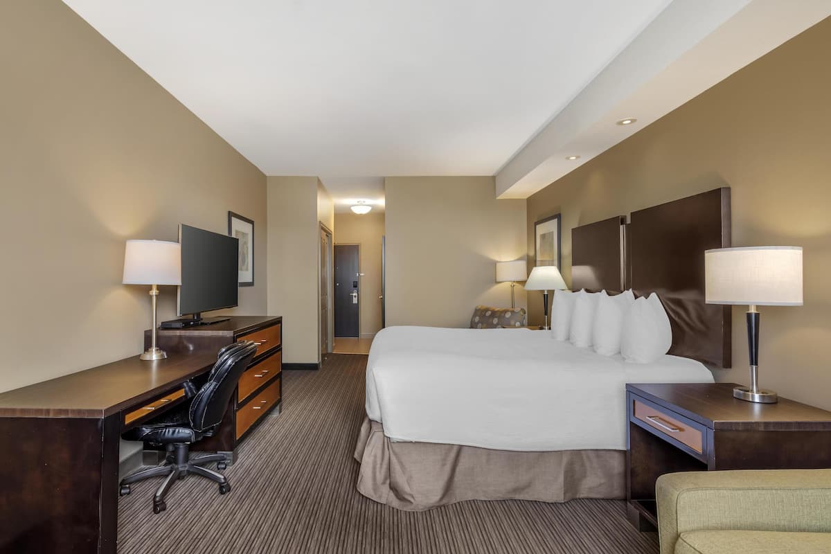 Quarto de hotel com uma cama grande, uma escrivaninha com cadeira, uma televisão e duas luminárias de cabeceira.