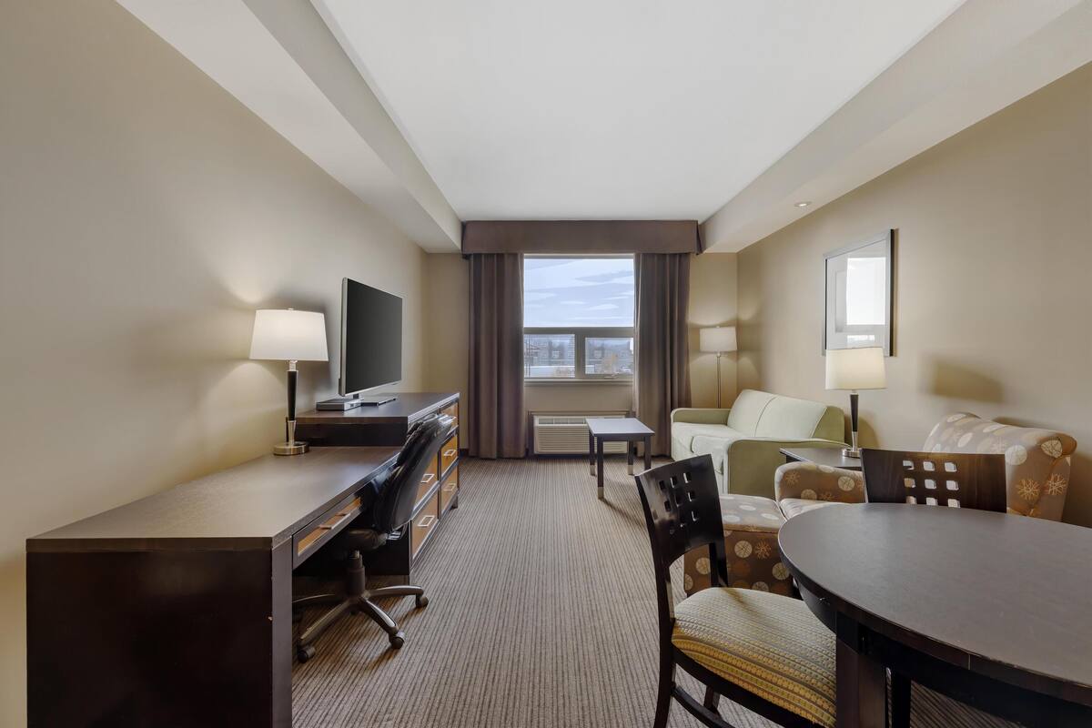 Quarto de hotel com escrivaninha, cadeira, televisão, sofá e mesa de jantar.