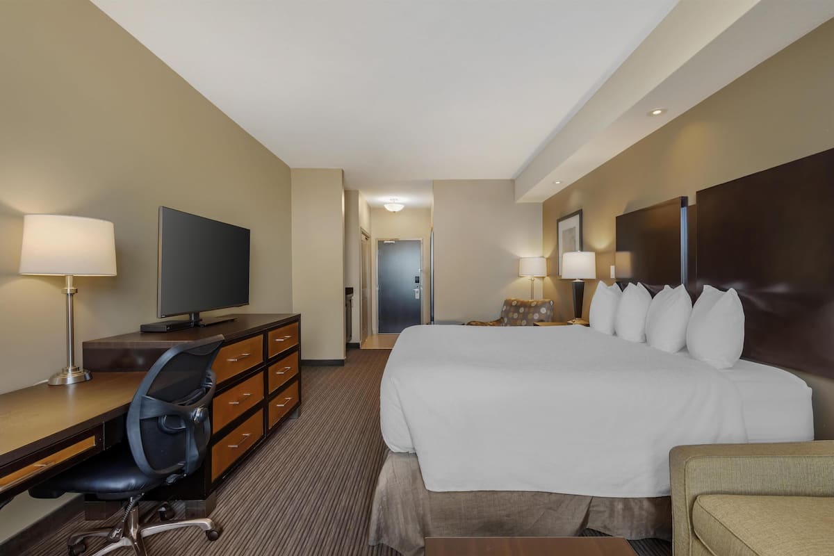 Quarto de hotel com uma cama grande, uma escrivaninha com cadeira, televisão e abajur.