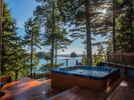 Uma banheira de hidromassagem em deck de madeira, com vista para uma floresta e um corpo d'água.