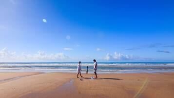 Uma praia com céu claro, ondas do oceano e pessoas caminhando.