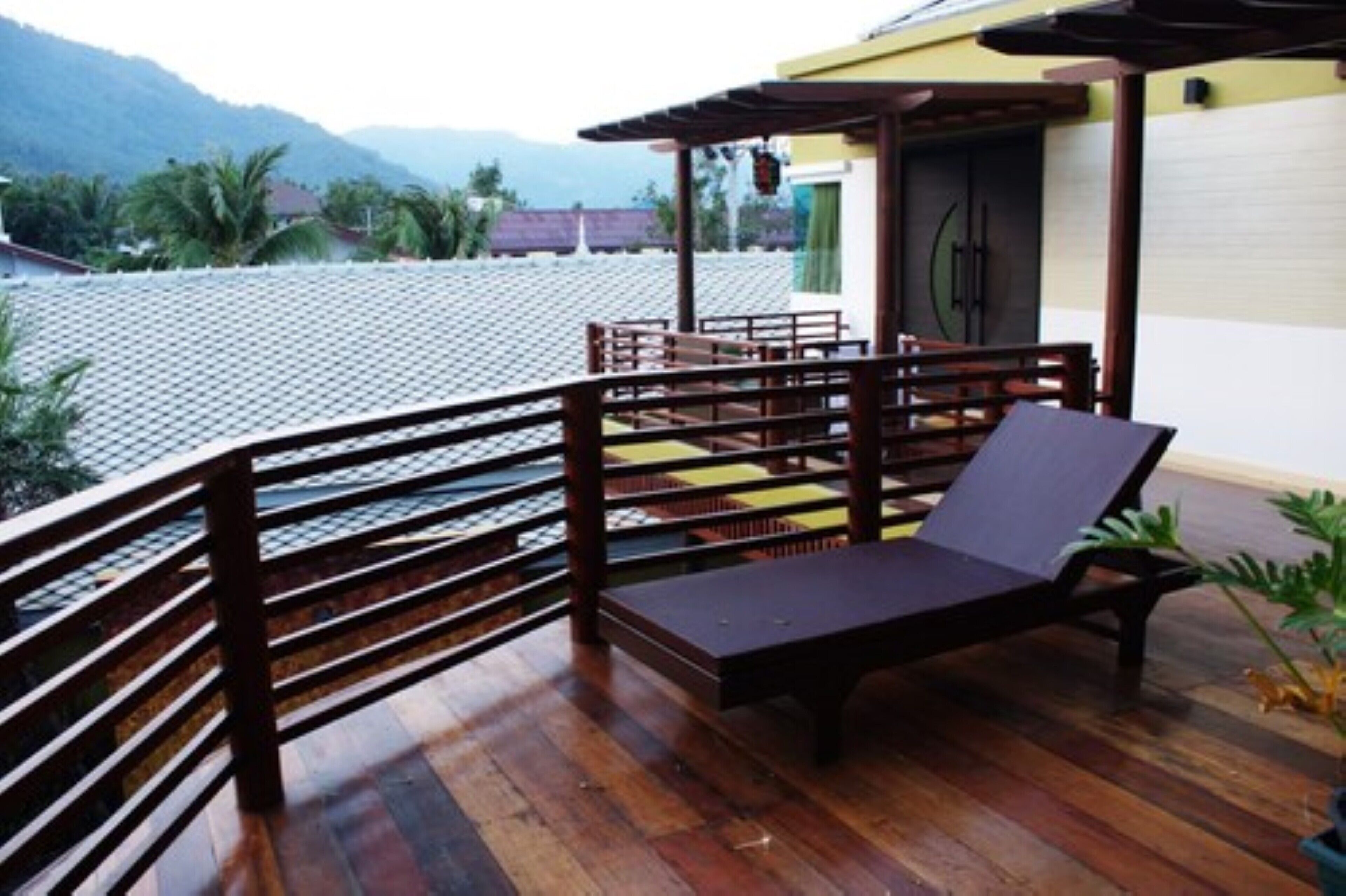 Um deck de madeira com uma única cadeira de descanso e uma mesa pequena, com vista para uma paisagem montanhosa.