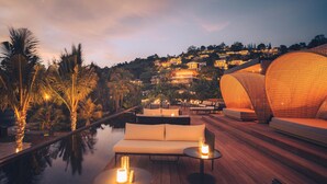 Um terraço tranquilo com lounge, piscina, espreguiçadeiras e vista para um resort na colina.