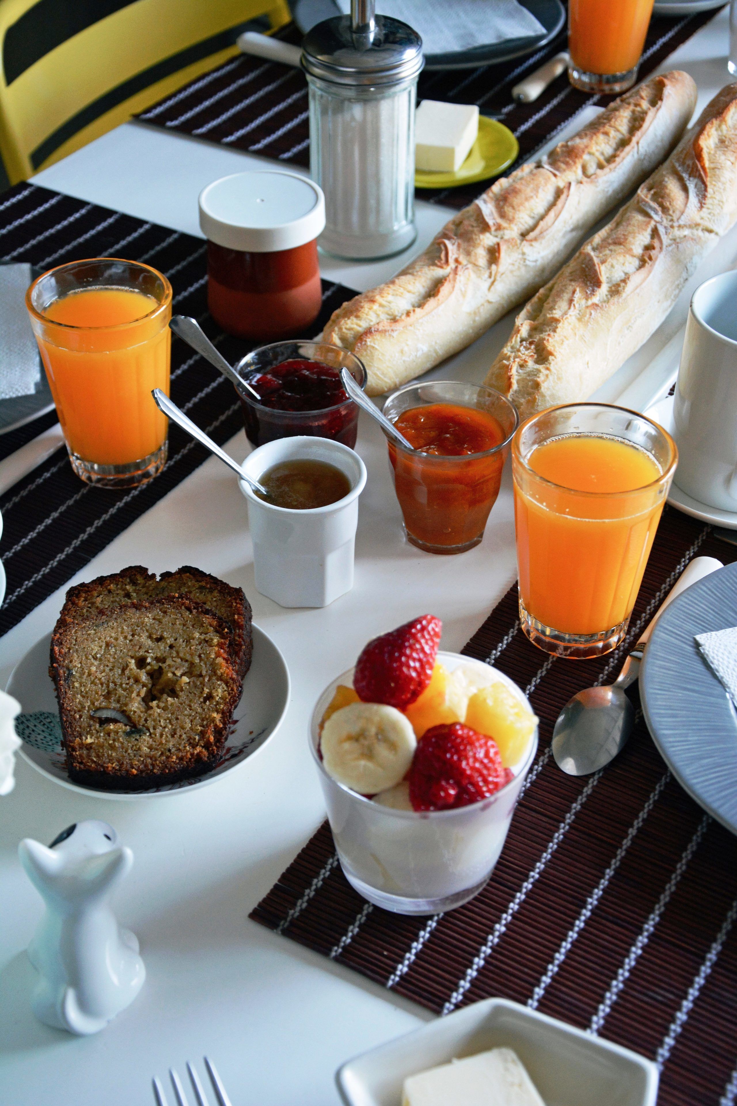 Uma mesa de café da manhã com pão, frutas e suco.