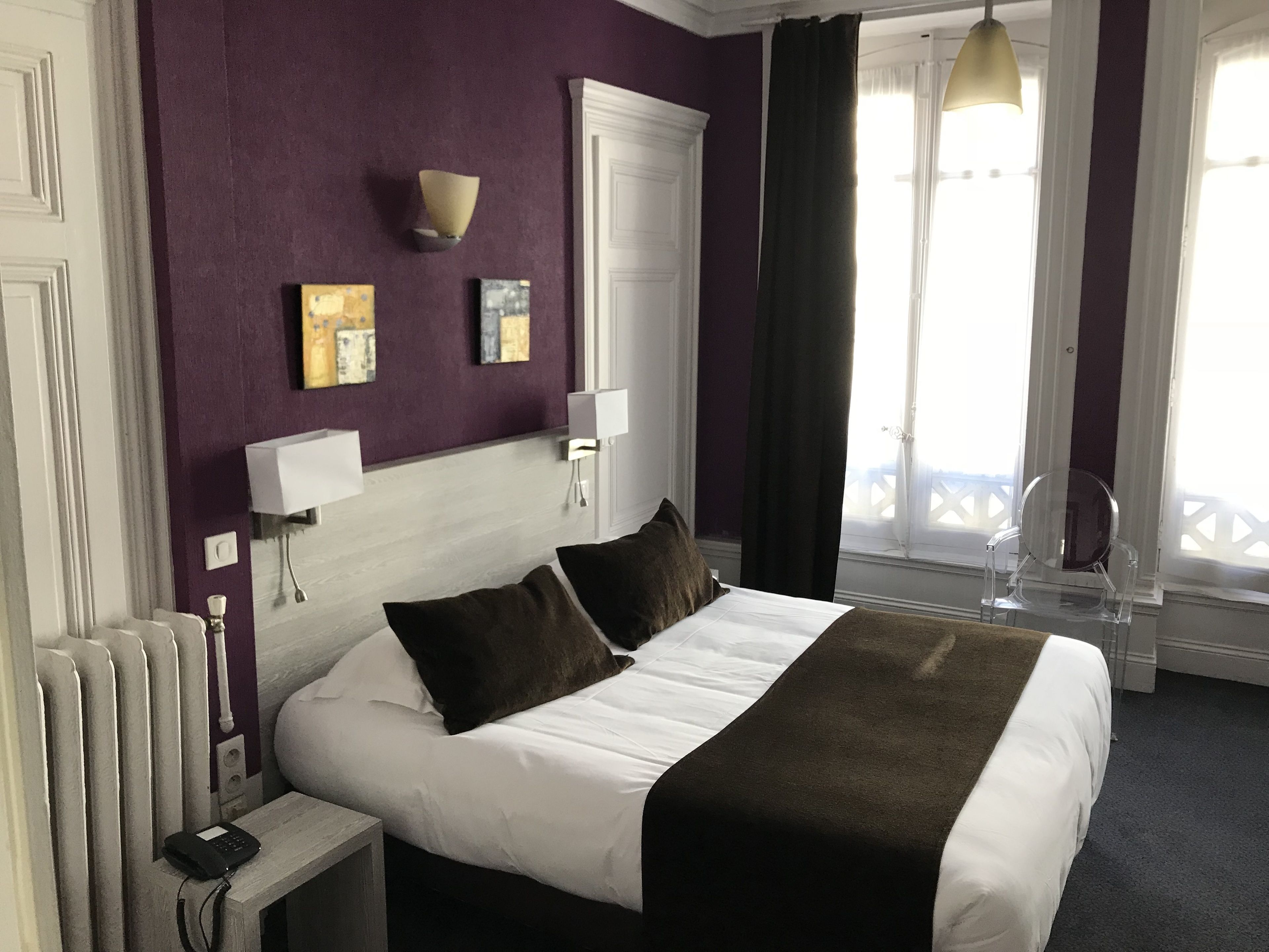 Quarto de hotel com cama, abajures, radiador, telefone, obras de arte na parede e vista para a varanda externa.