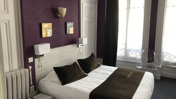 Quarto de hotel com cama, abajures, radiador, telefone, obras de arte na parede e vista para a varanda externa.