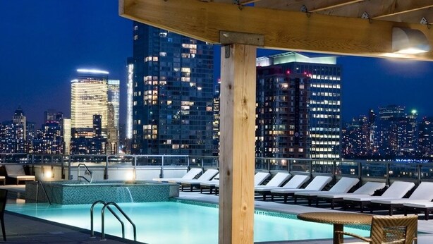 Uma área de piscina no terraço com espreguiçadeiras e vista para o horizonte da cidade à noite.