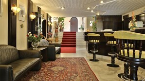 Um hall de hotel com sofá de couro, tapete estampado, escada e banquetas de bar.