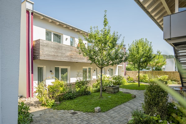 Um edifício moderno de dois andares com varanda, um jardim bem cuidado e um caminho pavimentado.