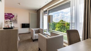 Quarto de hotel moderno com uma grande janela, televisão de tela plana, sofá, mesa de jantar e uma pintura decorativa de flores.