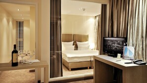 Quarto de hotel com uma cama, uma escrivaninha com computador, uma garrafa de vinho e copos.