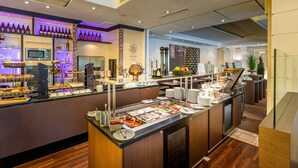 Uma área de buffet com diversos pontos de comida, um bar com garrafas e uma parede decorativa.