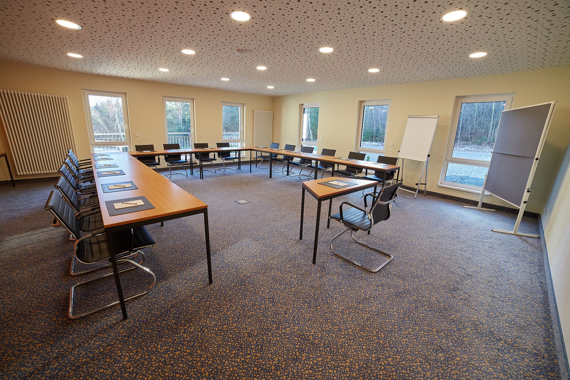 Uma sala de conferências com uma mesa comprida, cadeiras, um quadro branco e grandes janelas.