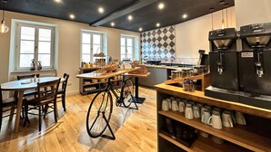 Um café com mesa e cadeiras de madeira, uma bicicleta e máquinas de café.
