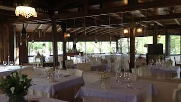 Um espaço de refeições interno com mesas preparadas para o serviço, grandes janelas e luminárias pendentes.