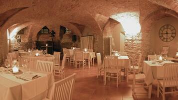 Restaurante com arcos de tijolo, mesas brancas e iluminação de velas.