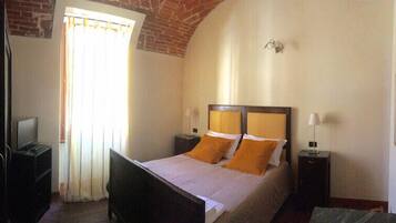 Quarto com uma cama, televisão e janela com cortinas.
