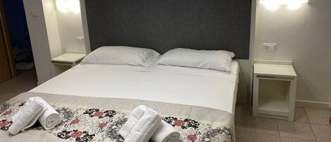 Cama bem arrumada com lençóis brancos e duas toalhas enroladas sobre o lençol.