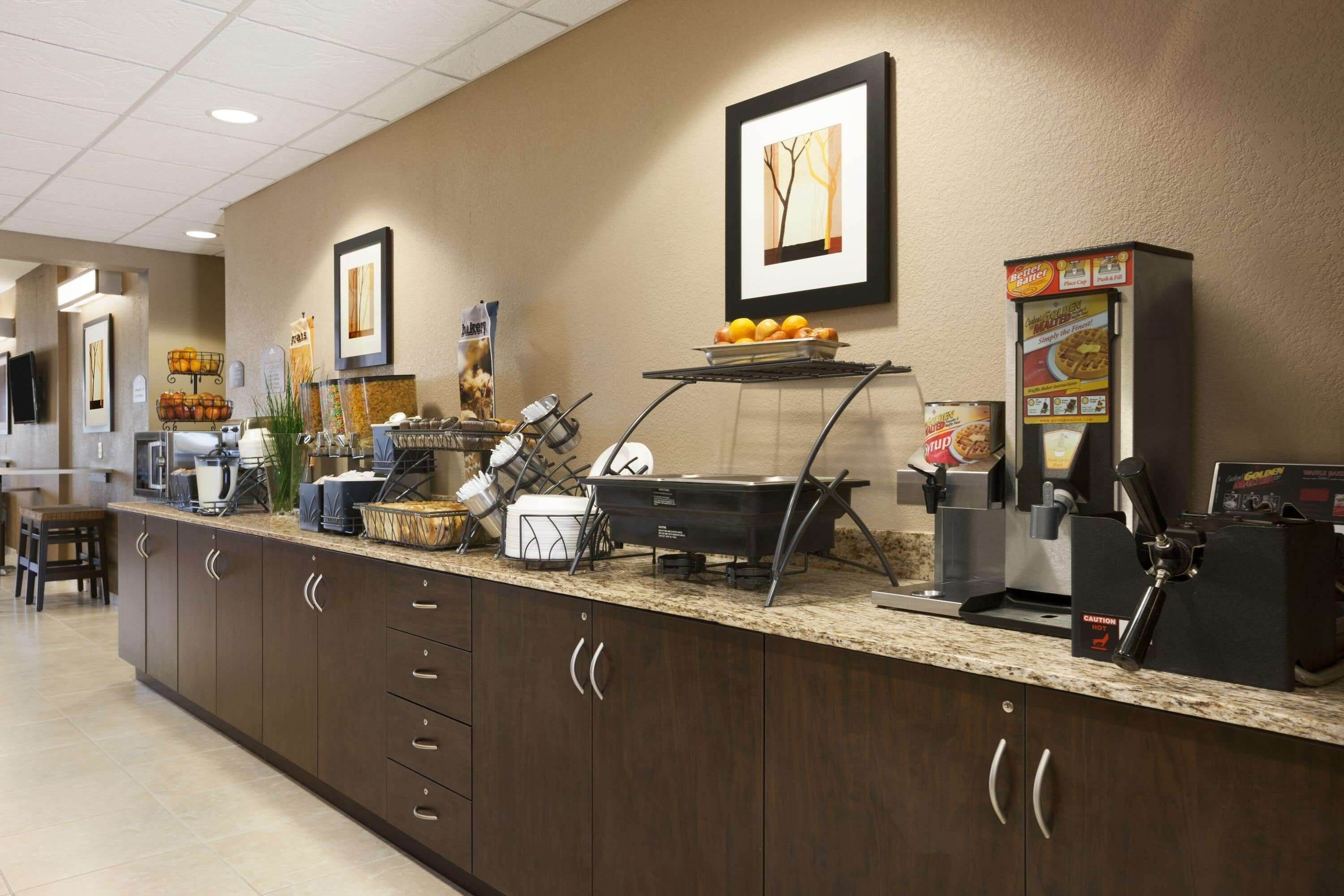 Espaço de pequeno-almoço de hotel com buffet, incluindo máquina de café, cesta de frutas e um sinal de alerta.