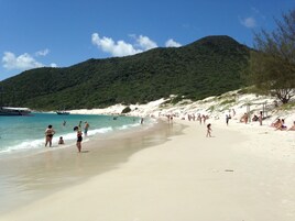 Uma praia com pessoas, um barco e uma colina ao fundo.