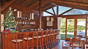 Uma área de bar com balcão de madeira, uma árvore de Natal, banquetas e uma mesa de jantar com cadeiras.