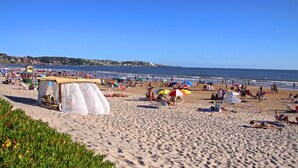 Uma praia com uma estrutura tipo tenda, guarda-sóis e pessoas relaxando.