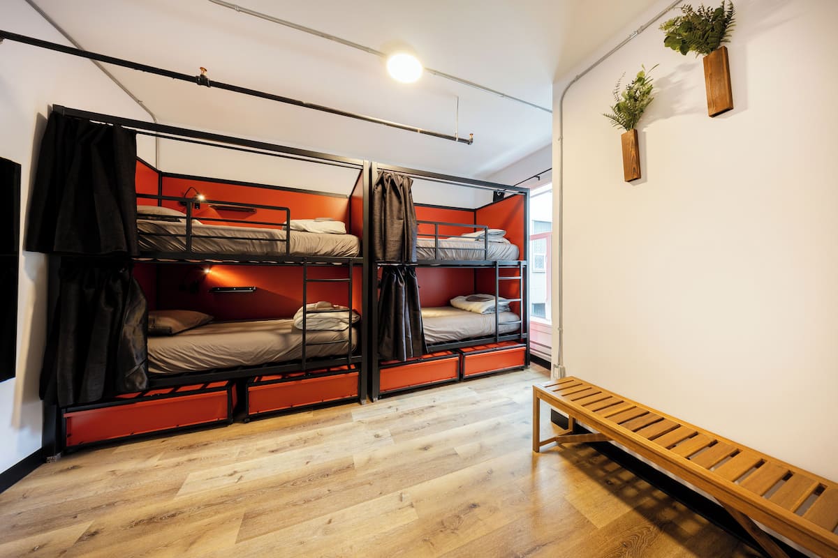 Quarto com beliche, piso de madeira, um banco e dois vasos fixados na parede.