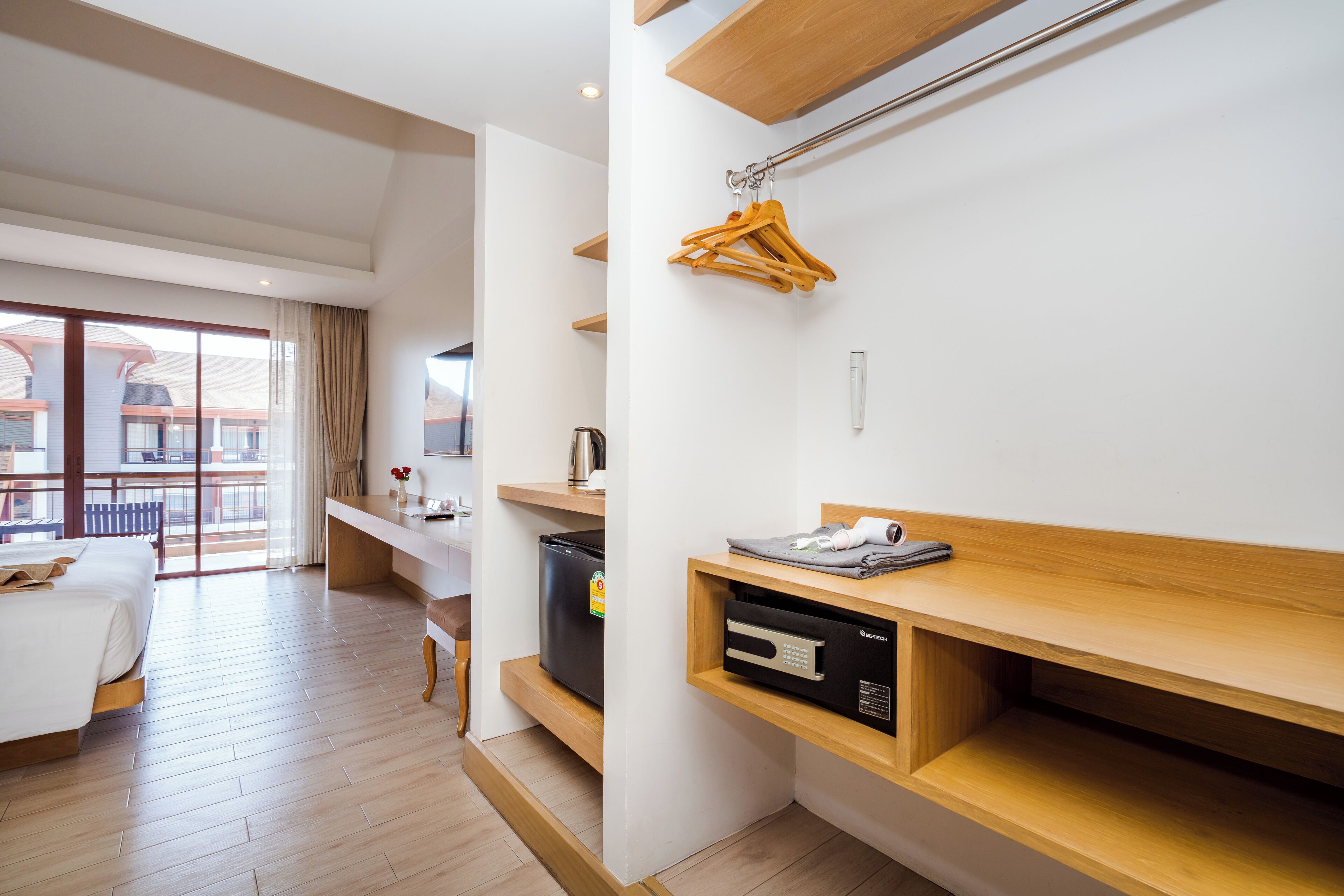 Quarto de hotel moderno com piso de madeira, uma cama, escrivaninha com computador, máquina de café e vista para a varanda externa.