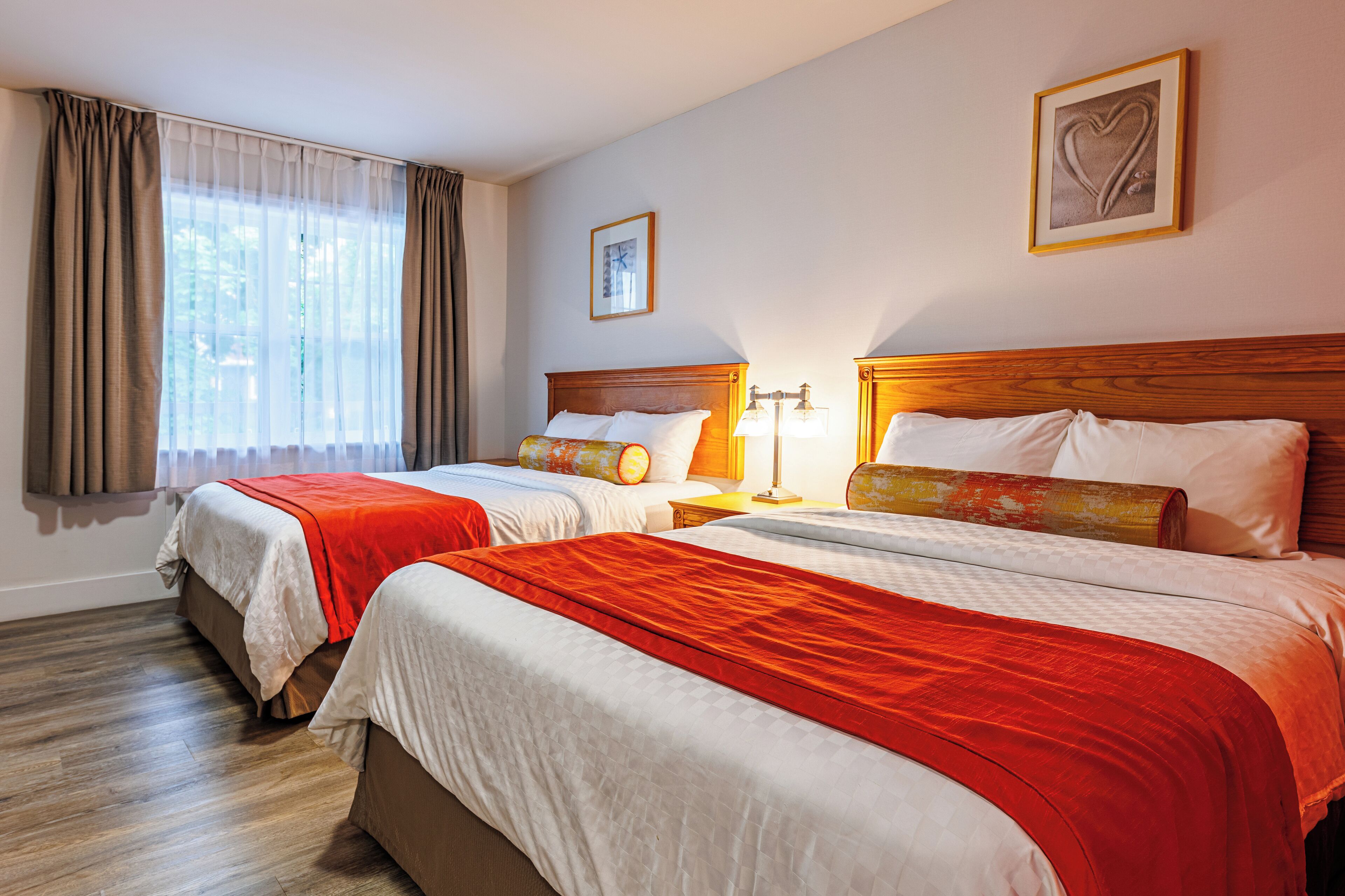 Quarto de hotel com duas camas, cabeceiras de madeira e uma janela grande com cortinas.