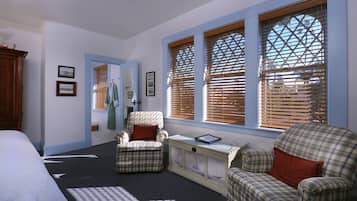 Quarto com cama, duas poltronas xadrez, cômoda e janela com persianas.
