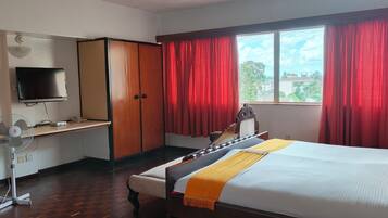 Quarto de hotel com uma cama, uma escrivaninha com televisão, um guarda-roupa e uma janela com cortinas vermelhas.