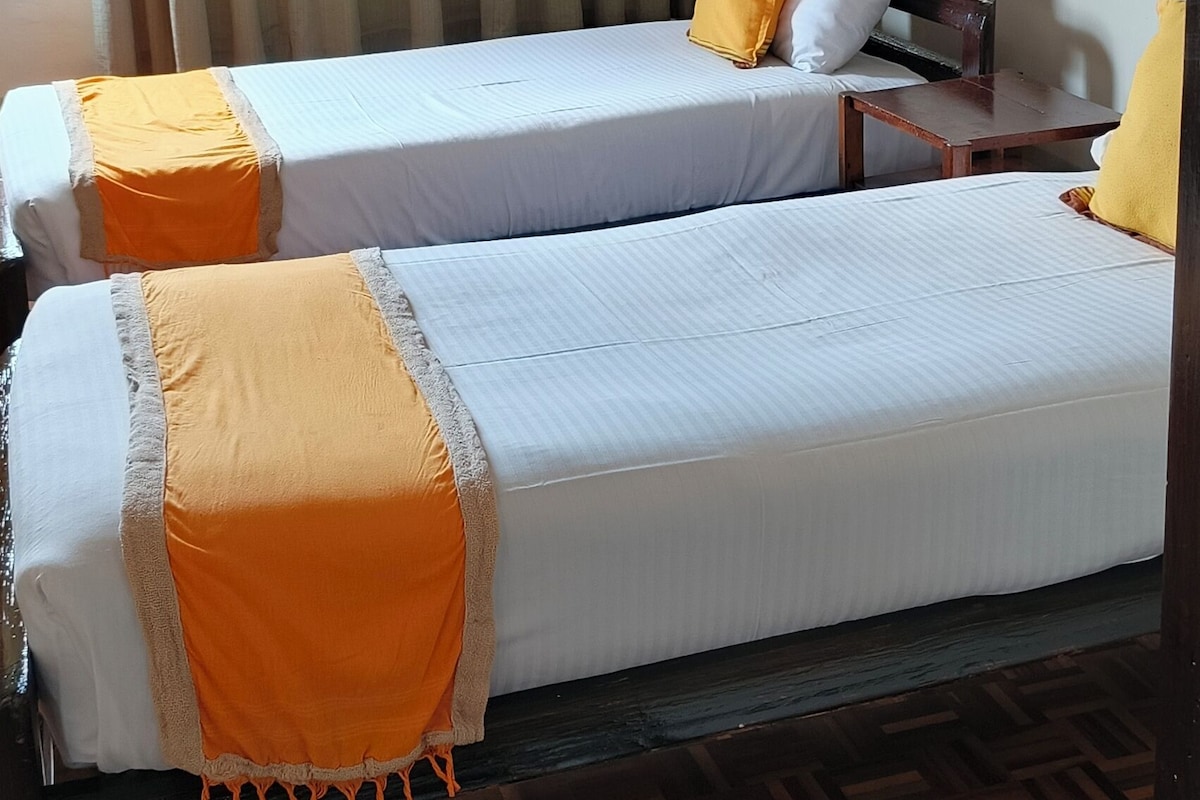 Quarto de hotel com duas camas, piso de madeira, janela com cortinas e um quadro na parede.