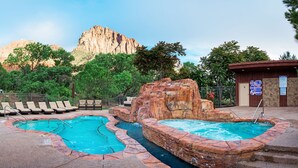 Uma área de piscina com espreguiçadeiras e uma banheira de hidromassagem, emoldurada por uma paisagem natural com uma montanha ao fundo.